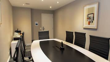 Uma sala de conferência com uma mesa comprida, cadeiras pretas e um quadro emoldurado na parede.
