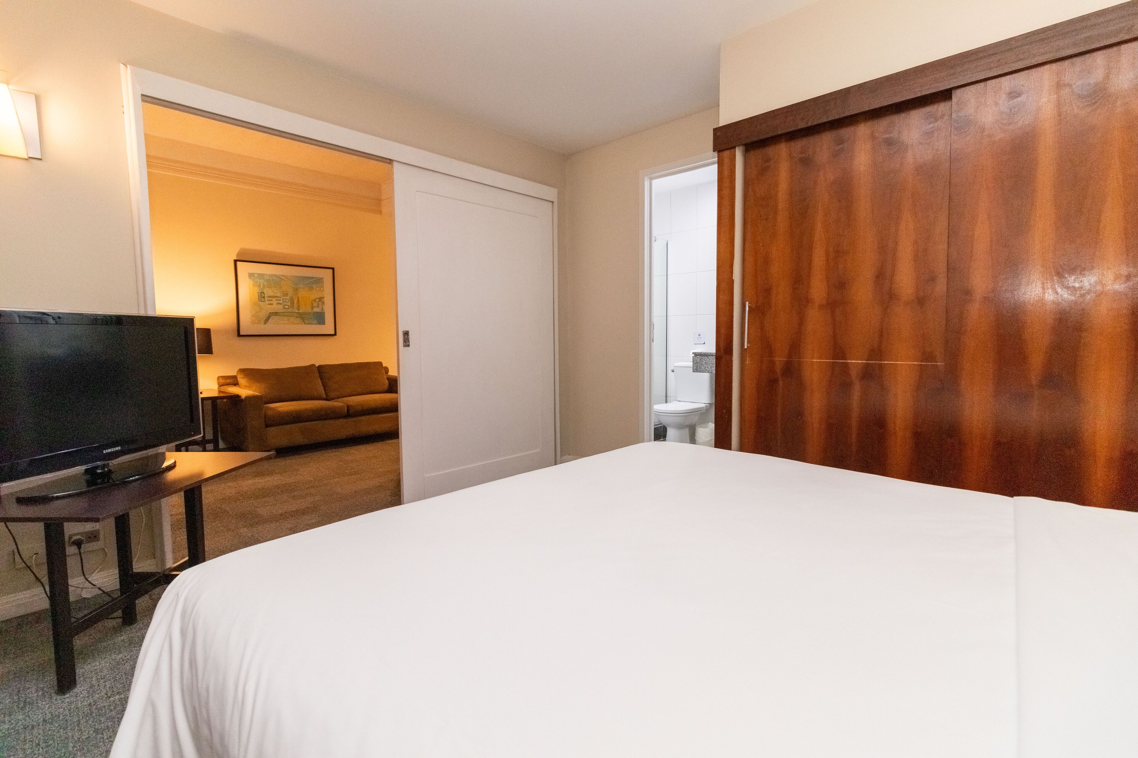Quarto de hotel com cama, televisão em móvel, sofá e porta de madeira.