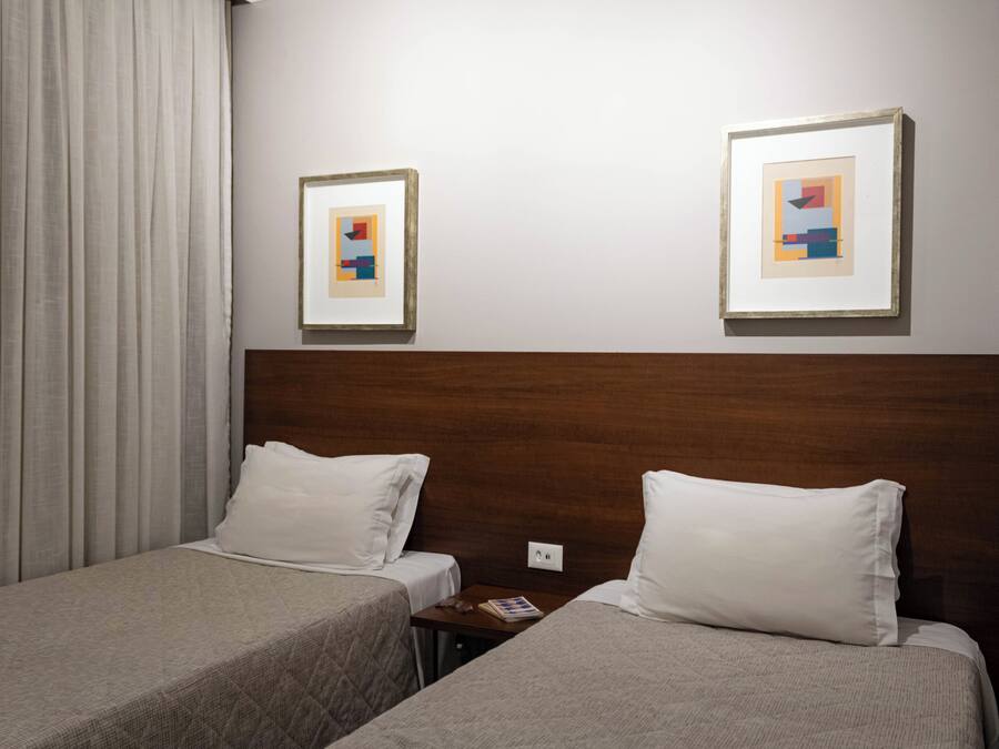Quarto de hotel com duas camas, cabeceira de madeira e duas obras de arte emolduradas na parede.
