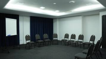 Uma sala de conferências com um quadro branco, cortinas escuras e uma fileira de cadeiras.