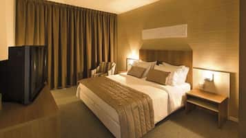 Quarto de hotel com cama grande, televisão, escrivaninha e mesa de cabeceira.