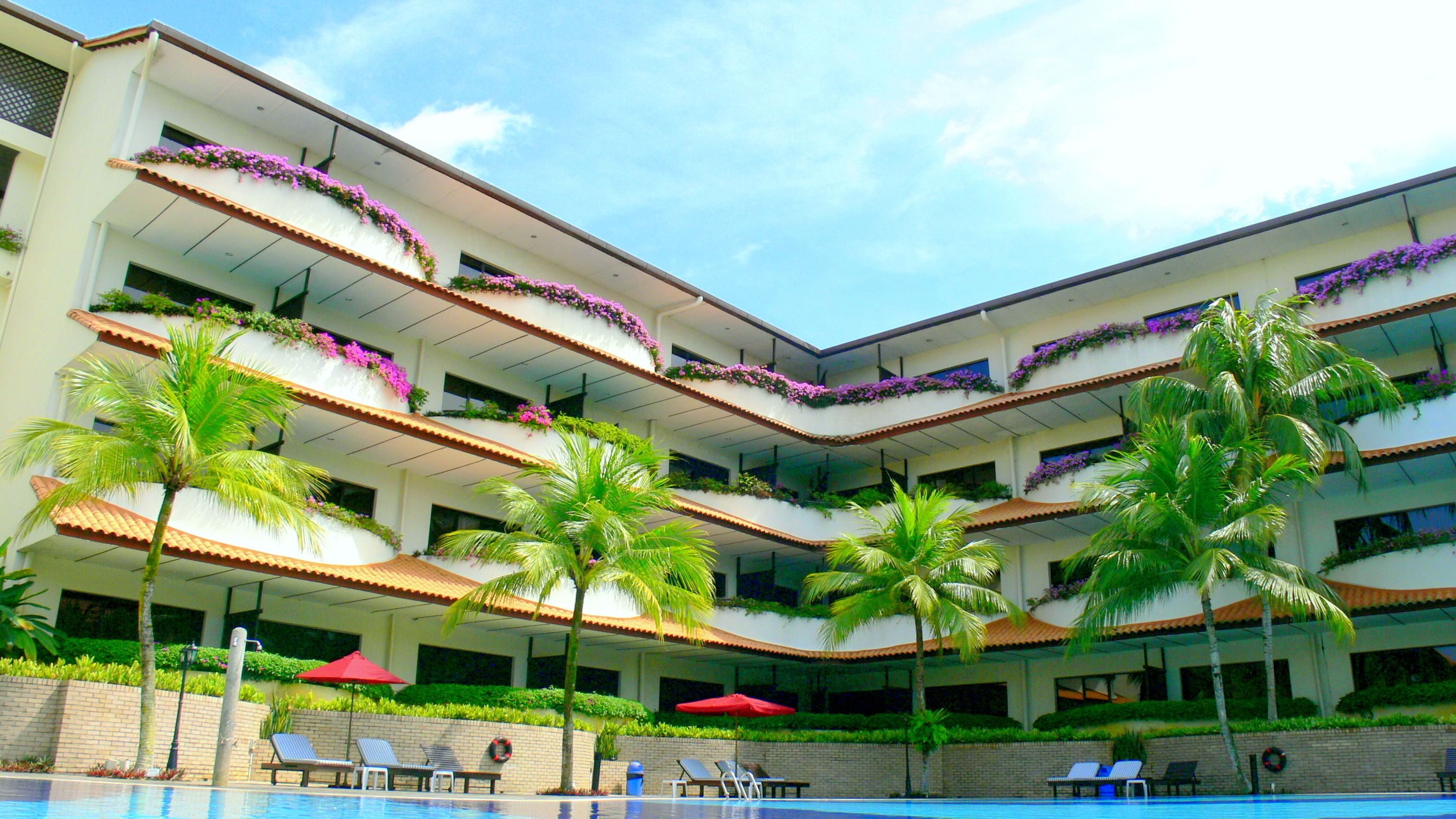 Um hotel com várias varandas decoradas com flores, piscina e palmeiras.