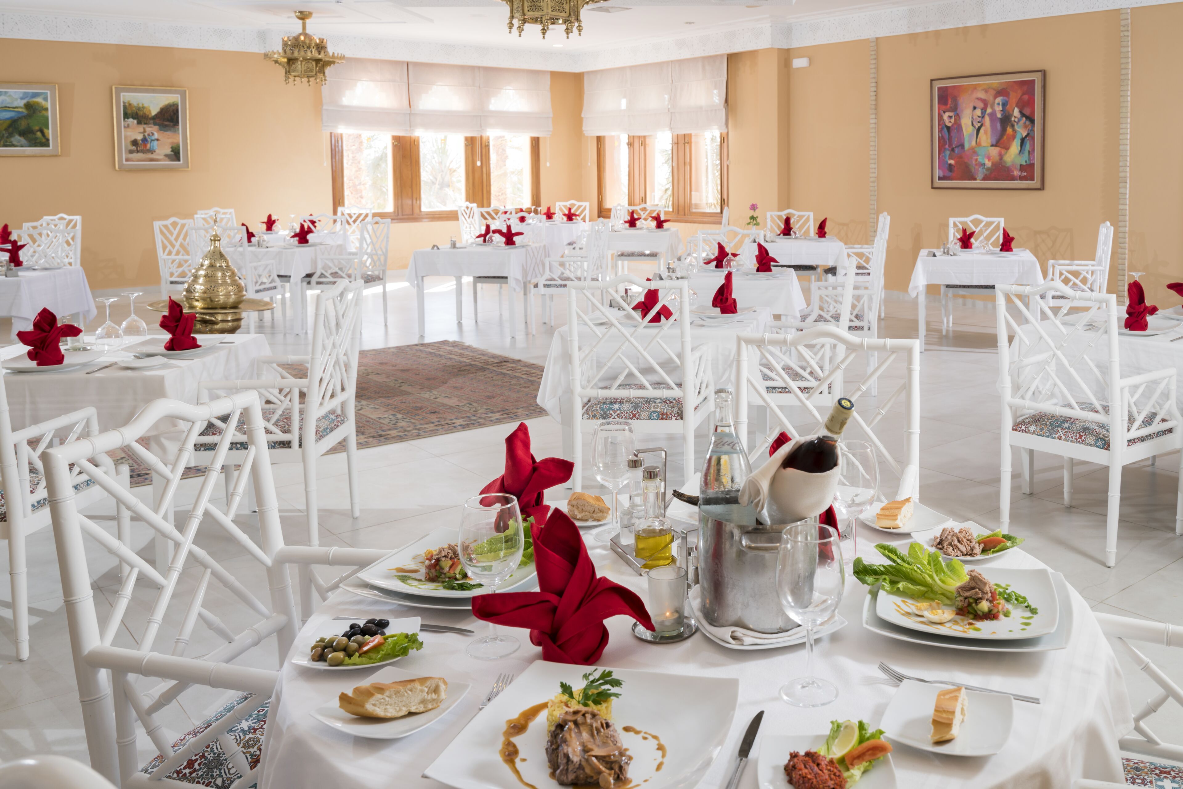Uma sala de jantar formal com mesas e cadeiras brancas, dispostas para uma refeição.
