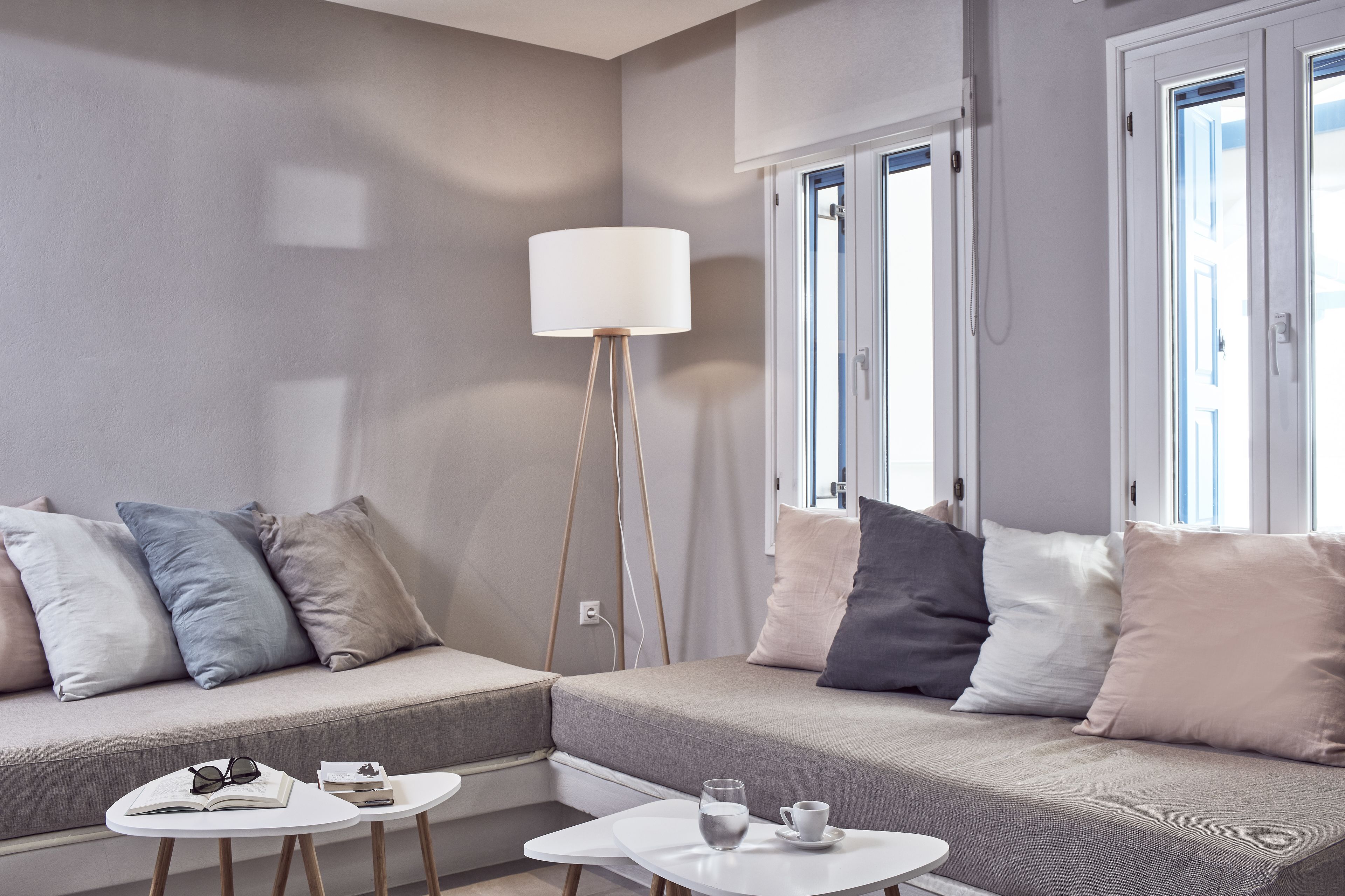 Uma sala de estar moderna com um sofá, duas mesinhas laterais, um abajur e uma janela com persianas.