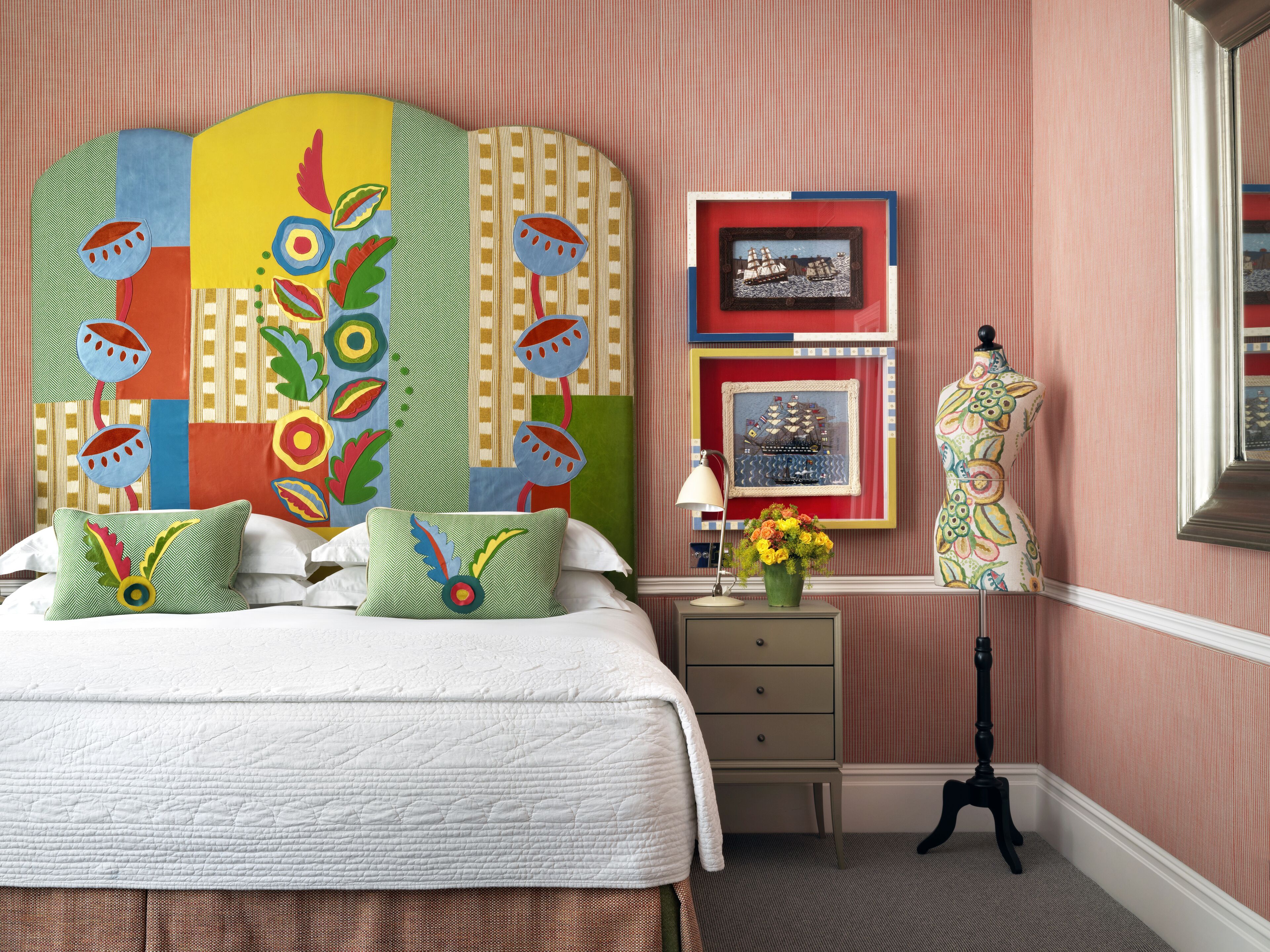 Quarto com uma cama grande, cabeceira colorida e cômoda com um vaso de flores.