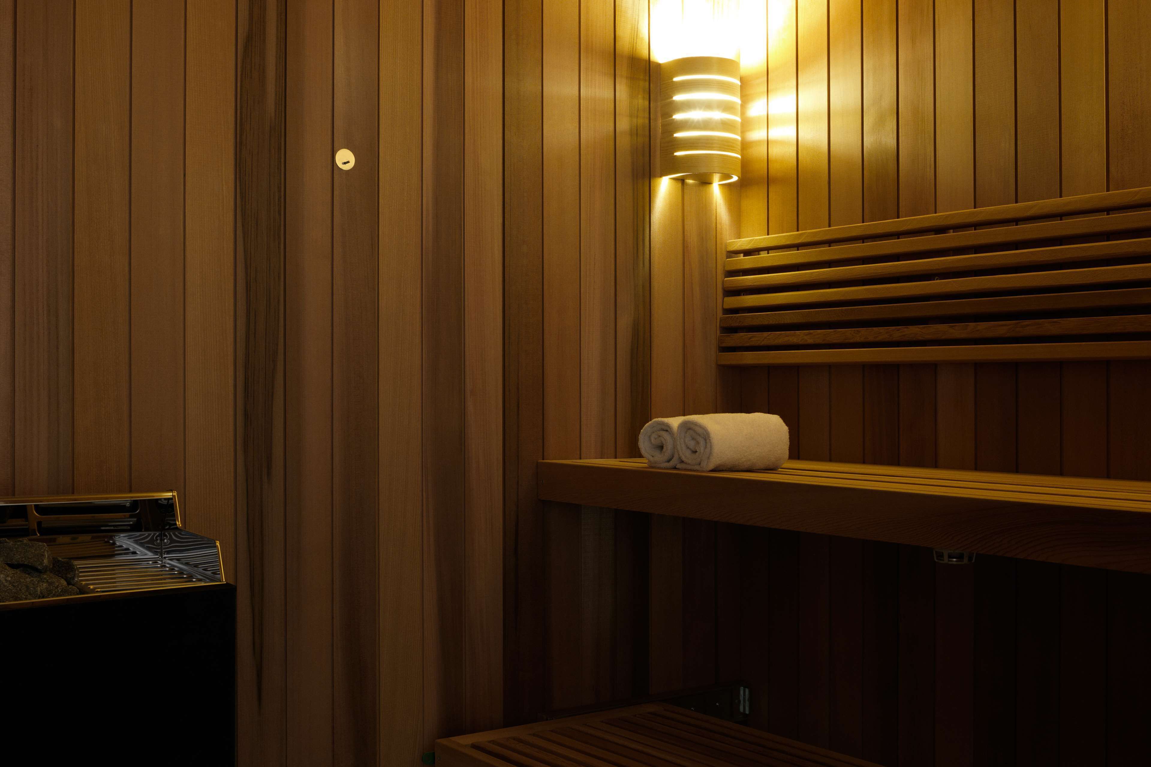 Uma sauna de madeira com um banco, uma prateleira com toalhas e uma luminária fixada na parede.