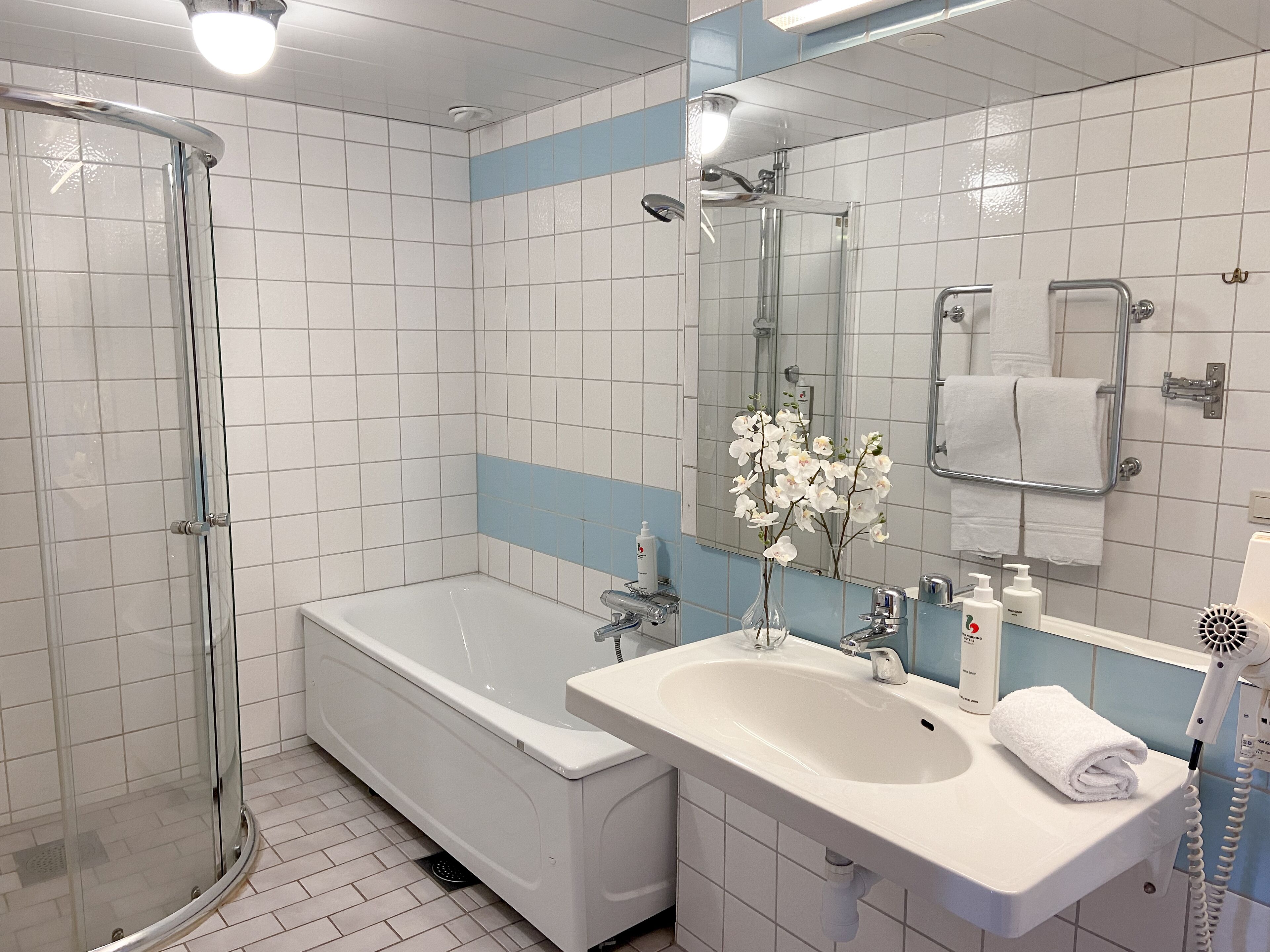 Uma casa de banho moderna com chuveiro envidraçado, banheira branca e lavatório com toalha.