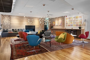 Uma sala de estar moderna com lareira, cadeiras coloridas e uma grande obra de arte abstrata na parede.