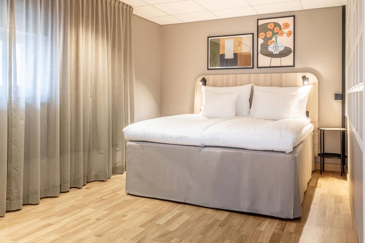 Quarto de hotel moderno com uma cama grande, piso de madeira e duas obras de arte emolduradas na parede.