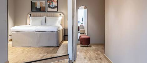 Quarto de hotel com cama, espelho, uma cadeira vermelha e piso de madeira.