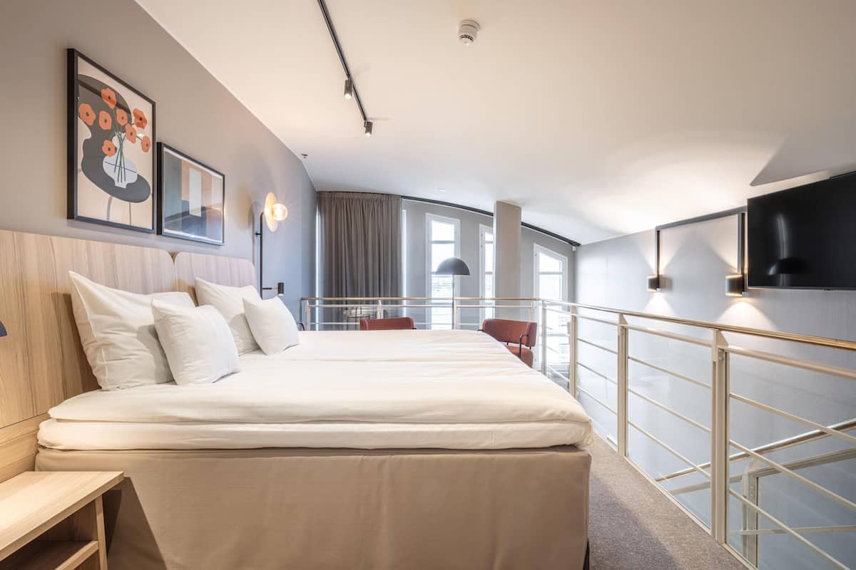 Quarto de hotel com cama, mesas de cabeceira, televisão, varanda com guarda-corpo e janela.