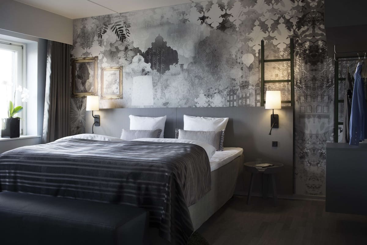 Quarto de hotel moderno com uma cama grande, uma mesa pequena e um guarda-roupa.