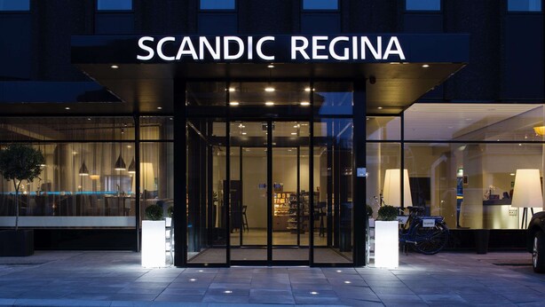Exterior do hotel Scandic Regina com entrada de vidro, uma bicicleta estacionada e um letreiro sobre a entrada.