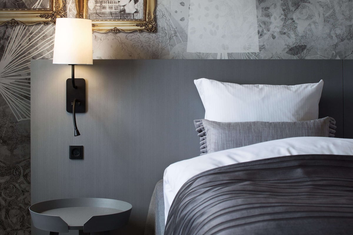 Quarto de hotel bem arrumado com cama, abajur, mesa redonda pequena e telefone fixado na parede.