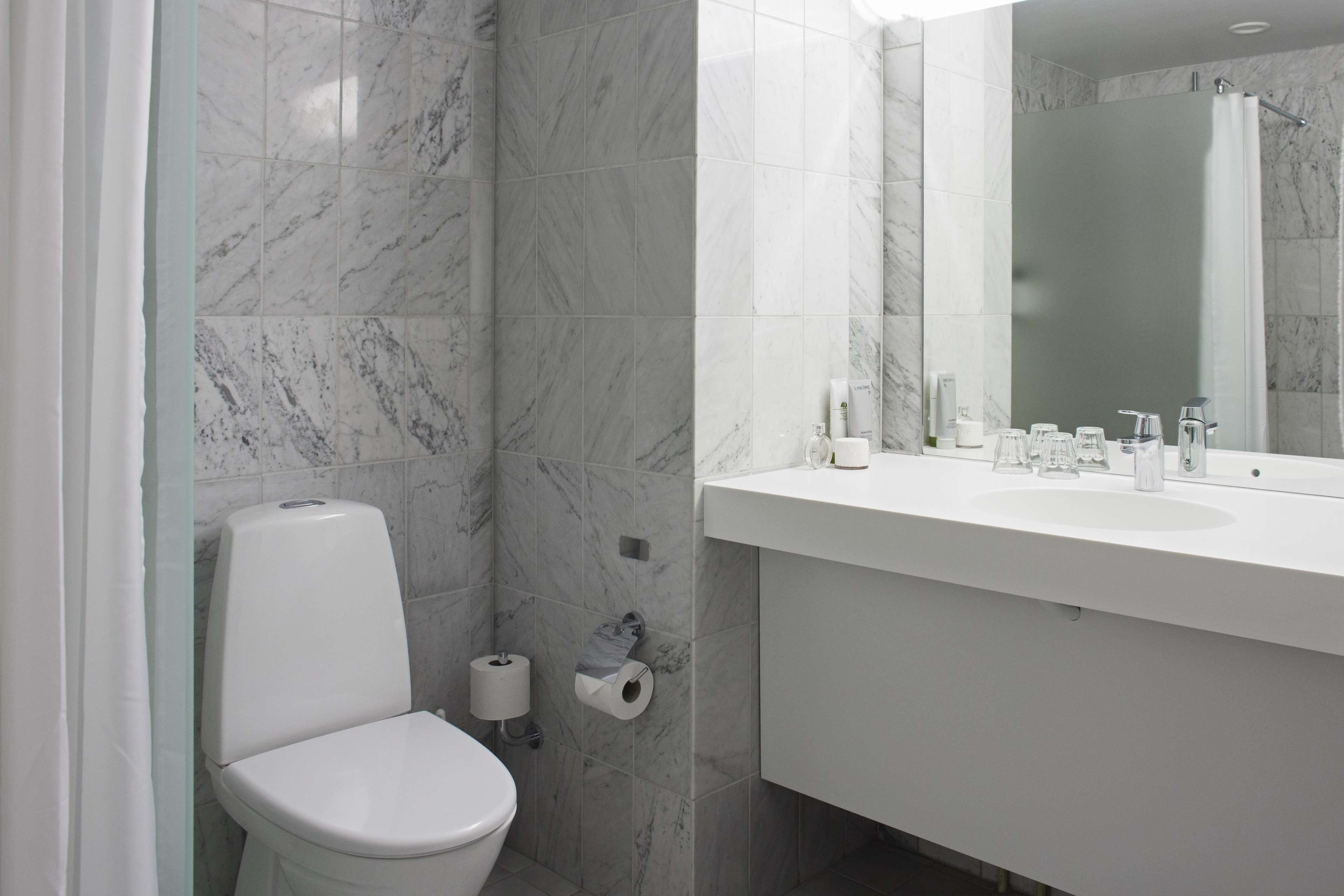 Um banheiro com vaso sanitário, azulejos de mármore, pia e espelho.