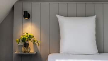Quarto com cama, planta na mesa de cabeceira, luminária na parede e prateleira.