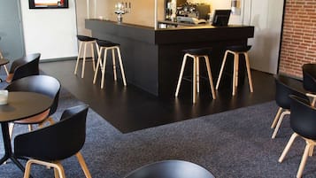 Uma área de estar moderna com mesas redondas e cadeiras pretas, um balcão de bar com banquetas e uma parede de tijolos.