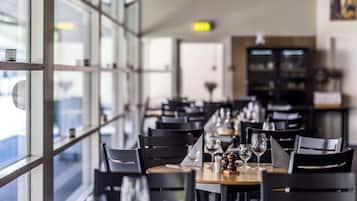 Um restaurante com uma mesa comprida posta para refeições, grandes janelas e decoração de interiores moderna.