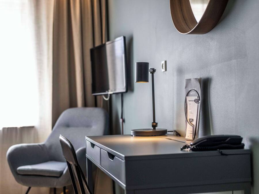 Quarto de hotel moderno com uma escrivaninha, uma cadeira, uma TV de tela plana, um abajur, um telefone e um cartão de segurança na parede.