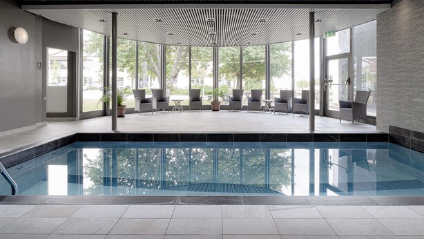 Uma área moderna de piscina interna, com vista desobstruída para a piscina, área de estar e janelas amplas.