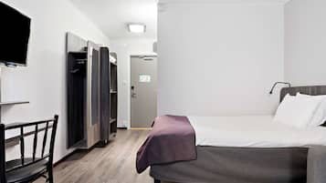 Quarto de hotel com cama, escrivaninha, cadeira, televisão e guarda-roupa.