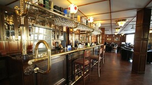 Uma área de bar com balcão de madeira, banquetas e copos pendurados.