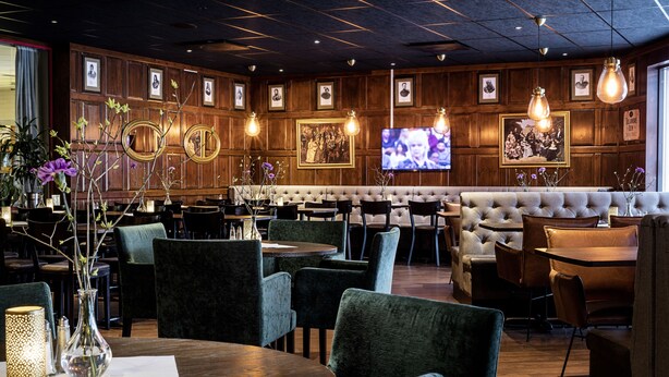 Restaurante com paredes de madeira, uma grande tela de televisão e diversas opções de assento, incluindo mesas redondas e cabines acolchoadas.