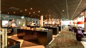 Um lobby de hotel moderno com um balcão de recepção central, áreas de estar e uma parede grande exibindo mapas e informações sobre a cidade.