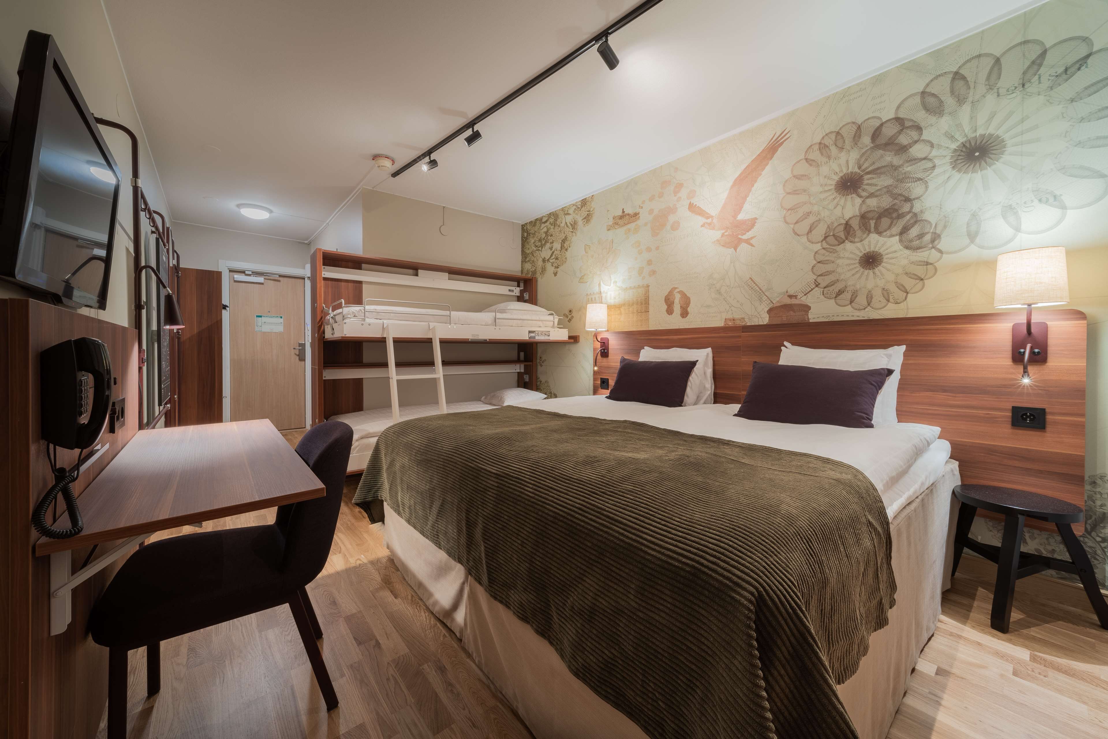 Quarto de hotel com cama, escrivaninha, cadeira, televisão e parede com mural floral.