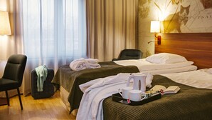 Quarto de hotel com duas camas, uma cadeira, roupão, bandeja com chaleira, chávenas e um livro.