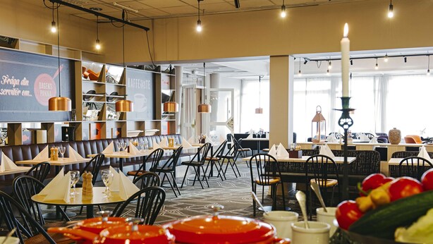 Um restaurante com mesas e cadeiras, área de bar e buffet com diversos alimentos.