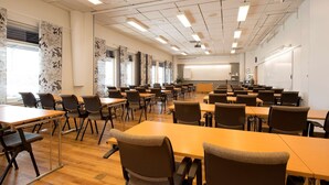 Uma sala de aula com fileiras de mesas e cadeiras, uma tela de projetor e um quadro branco.