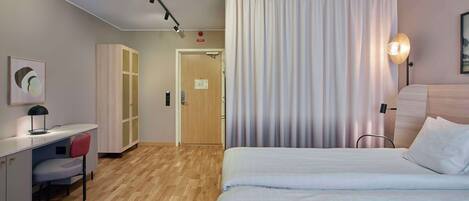 Quarto de hotel com cama, escrivaninha, cadeira, guarda-roupa e porta que dá para outro espaço.