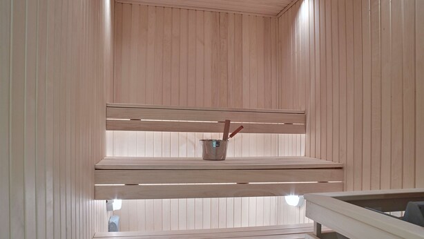 Uma sauna com bancos de madeira e um balde de metal com galhos.