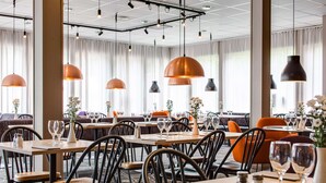 Um restaurante moderno com várias mesas, cadeiras pretas e laranja, e luminárias pendentes.