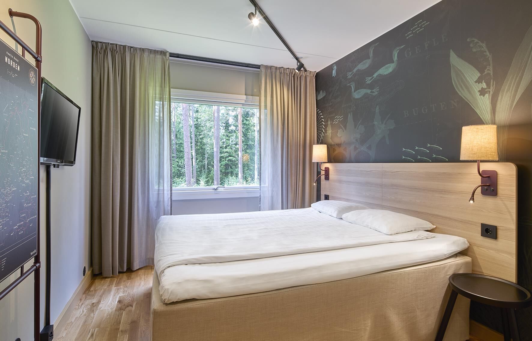 Quarto de hotel com uma cama grande, televisão, janela com cortinas e parede com um mapa.