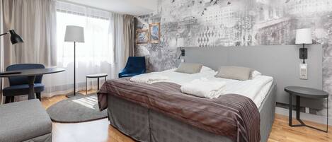 Quarto de hotel moderno com uma cama grande, uma mesa, uma cadeira e uma parede com um mural da paisagem urbana.