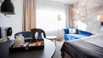 Quarto de hotel com uma cama, uma escrivaninha com luminária, uma cafeteira e uma mesinha.