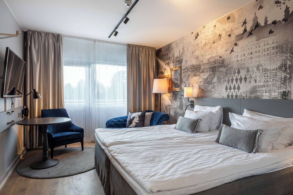 Quarto de hotel com uma cama grande, uma mesa, uma cadeira e uma televisão.