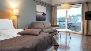 Quarto de hotel com cama, sofá, mesa pequena, televisão e janela com vista.