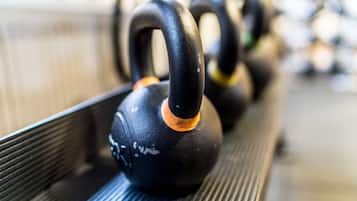 Diversos kettlebells pretos com detalhes laranja dispostos num suporte de metal.