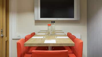 Uma sala de conferência com uma televisão de tela plana grande fixada na parede, uma mesa de madeira e cadeiras estofadas em laranja.