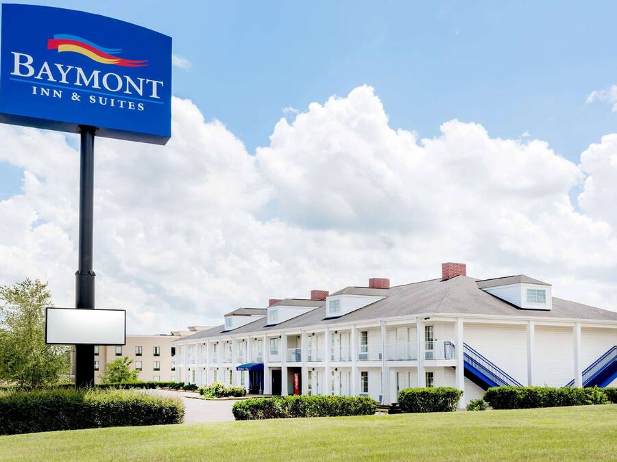 Edifício do Baymont Inn & Suites com grande placa, várias varandas e gramado bem cuidado.