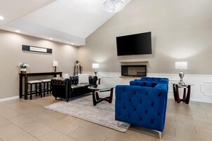 Uma sala de estar moderna com um sofá de couro preto, poltronas de veludo azul, uma TV de tela plana e uma lareira.