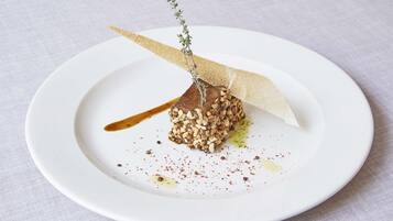 Um prato branco com sobremesa, nozes, um raminho de ervas e folha de ouro comestível.