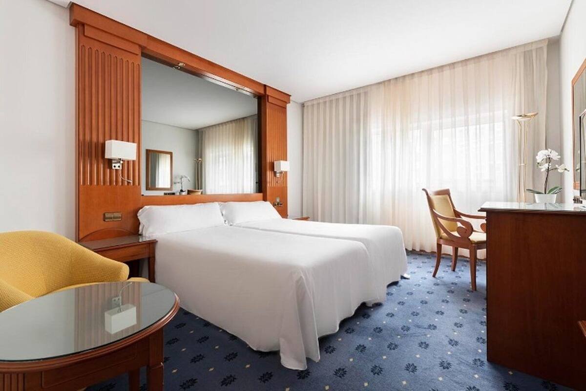 Quarto de hotel com duas camas, uma mesa, uma cadeira e uma pequena mesa.