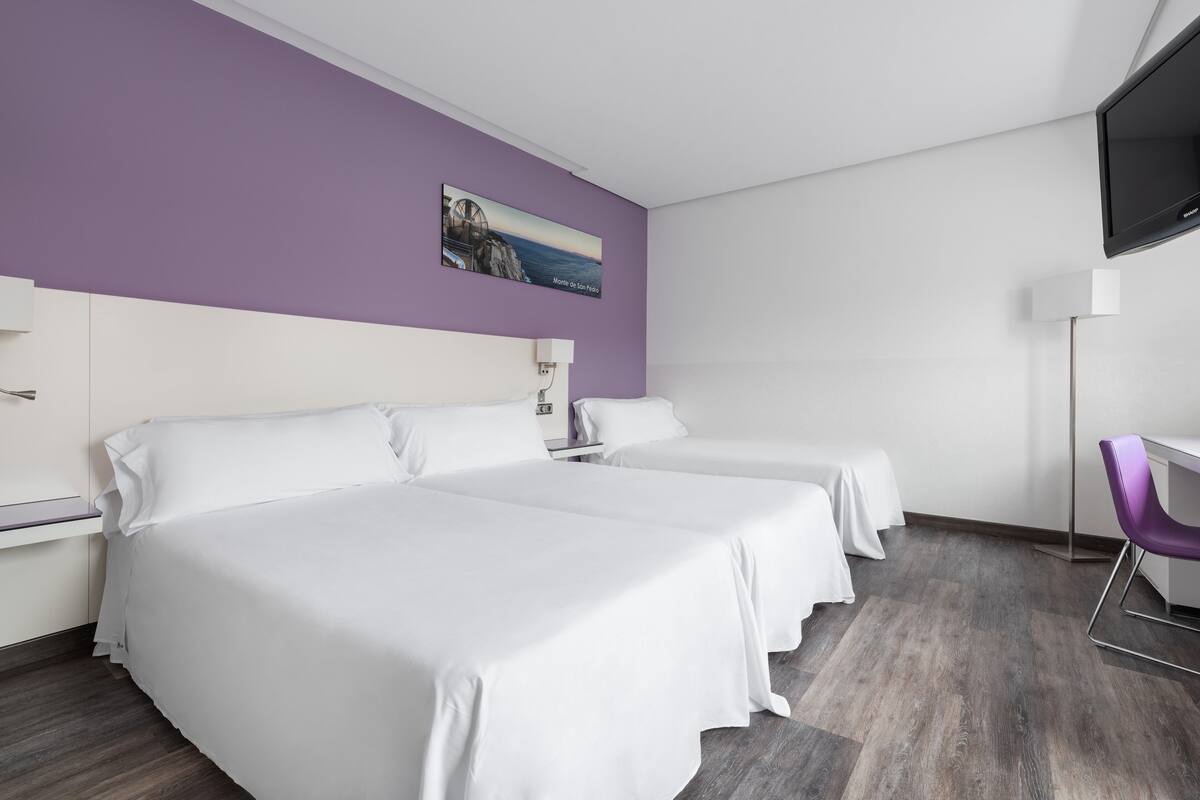 Quarto de hotel com duas camas, uma escrivaninha, uma cadeira, uma televisão e um quadro na parede.