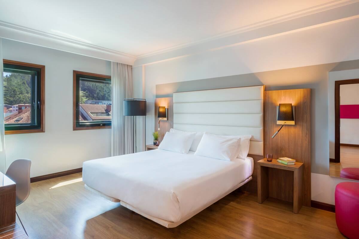 Quarto de hotel com cama grande, mesas de cabeceira, televisão e vista para o exterior.