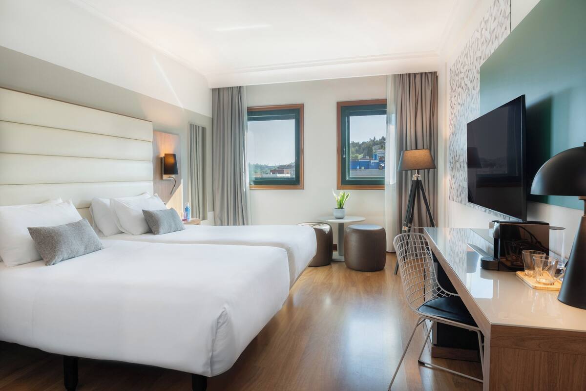 Quarto de hotel com duas camas, uma escrivaninha, televisão e vista para a cidade.