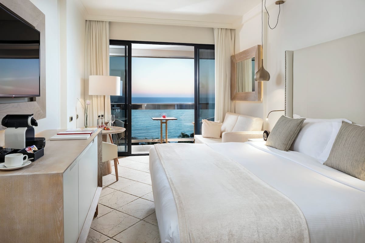 Quarto de hotel com uma cama grande, uma secretária com máquina de café, televisão e varanda com vista para o mar.